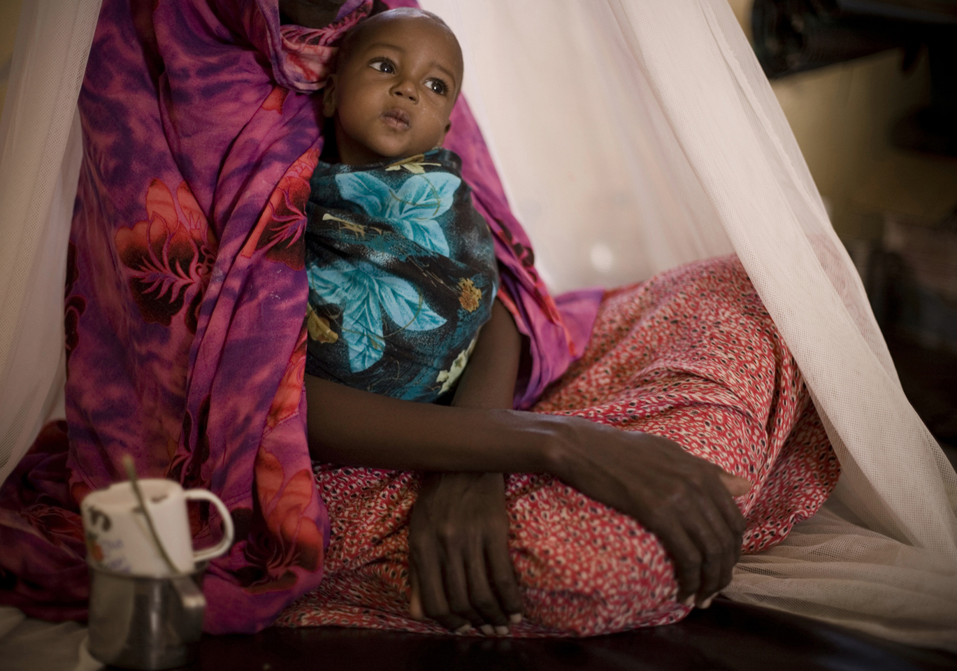 A small boy is held by his mother at the therapeutic feeding center of ...