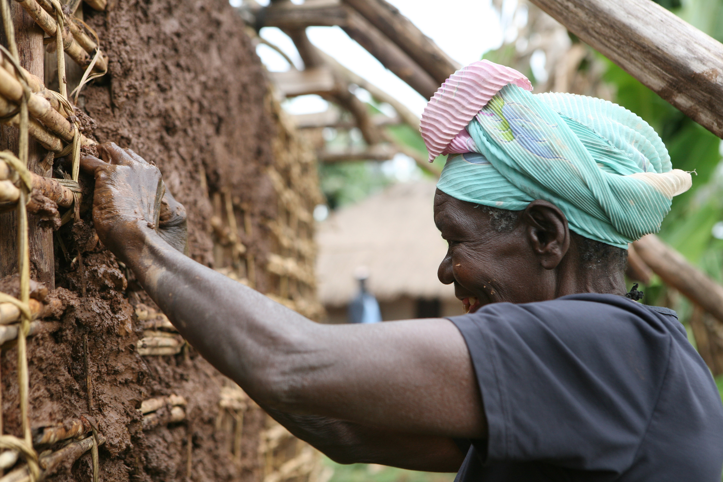 A woman applies mud to a new housing structure. In this area of Mahagi ...