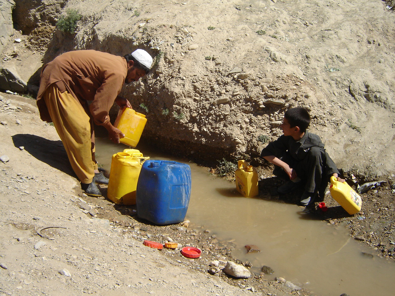A man and his son collect water from a canal on the side of a hill in ...